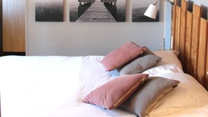Quarto com cama, almofadas, luminária pendente e obras de arte na parede.