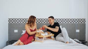Um casal sentado na cama com uma bandeja de itens de café da manhã e uma bebida.