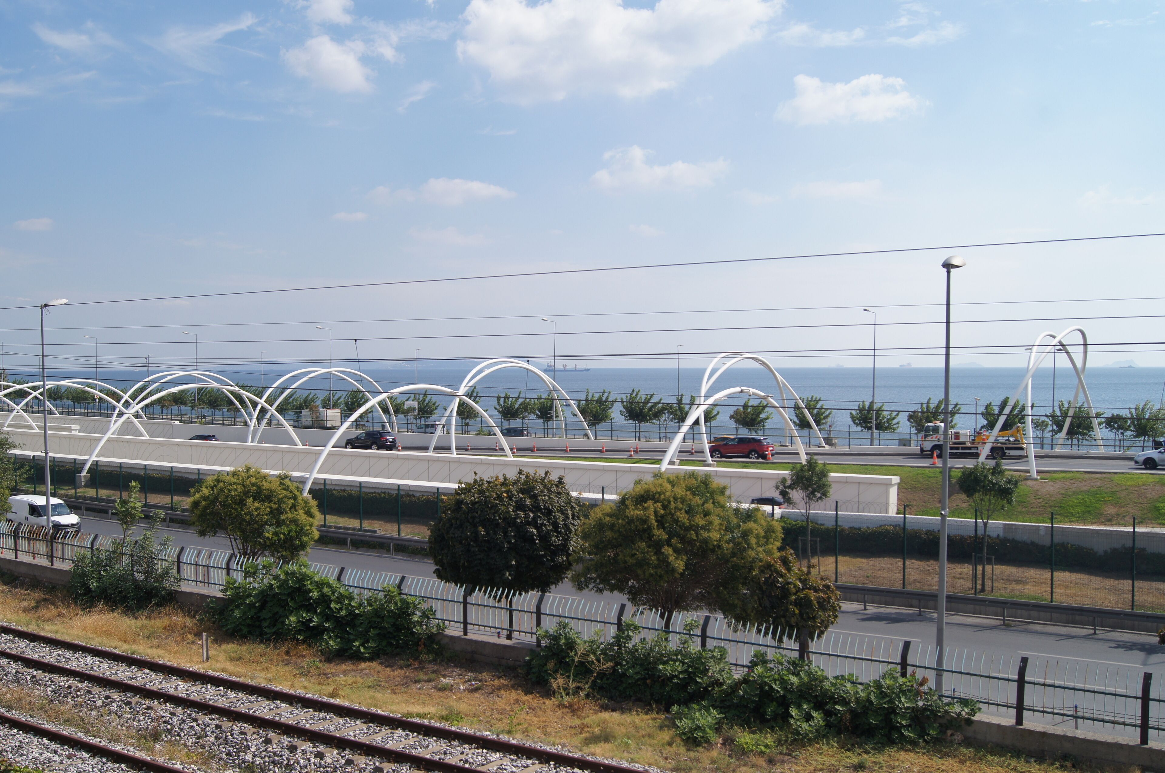 Uma ponte moderna com arcos brancos, uma estrada com carros e um corpo d'água ao fundo.