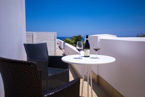 Varanda com cadeiras de vime e uma mesa pequena com garrafas de vinho e copos.