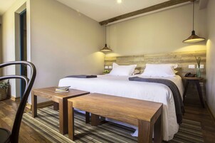 Quarto bem arrumado com cabeceira de madeira, cama com roupa de cama branca, mesa de cabeceira com luminária e uma cadeira.