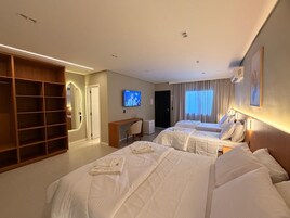 Quarto de hotel com duas camas, televisão, escrivaninha e guarda-roupa.