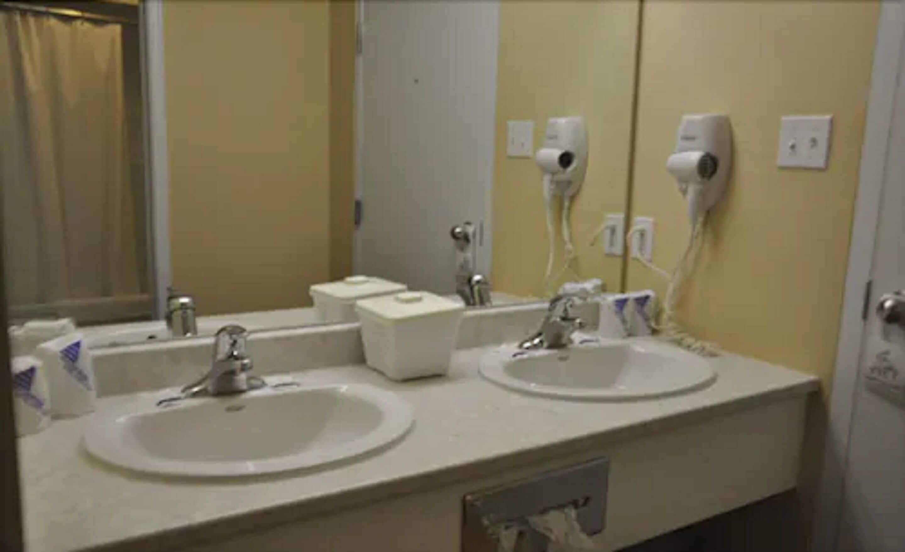 Casa de banho com duas pias, um espelho e um dispensador de toalhas.