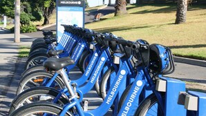 Uma fileira de bicicletas azuis com a marcação 'Melbourne', estacionadas em área designada.