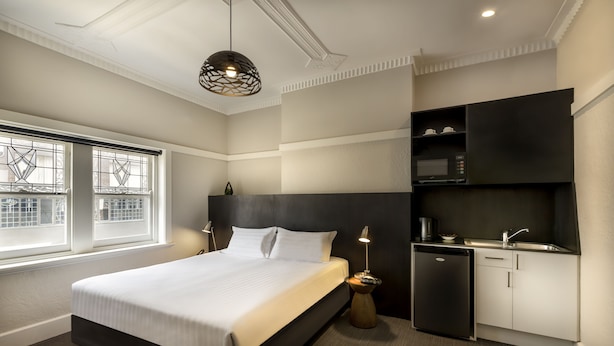 Quarto de hotel moderno com uma cama grande, cozinha planejada e janela com vista.