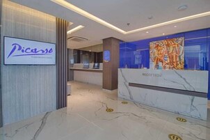 Uma área de recepção de hotel com um balcão de mármore, uma grande obra de arte de Picasso e uma placa do Hotel Picasso.