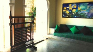 Quarto com um banco de madeira, um sofá verde com almofadas e uma pintura na parede.