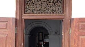 Uma entrada com porta de madeira e entalhes elaborados, dando acesso a um corredor com sofá e luminária.