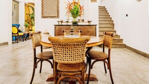 Uma sala de jantar com candelabro, mesa de madeira, cadeiras de vime e uma escada ao fundo.