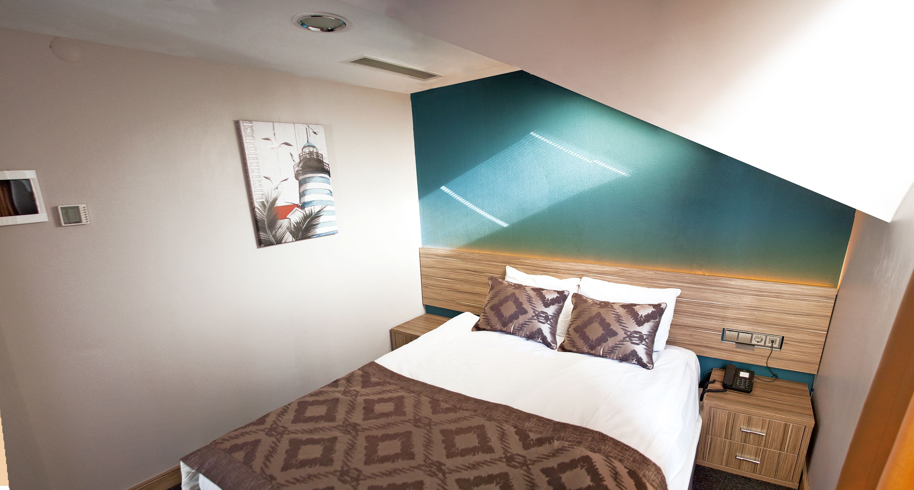 Quarto de hotel com uma cama, mesa de cabeceira, telefone fixado na parede e pintura de um farol.