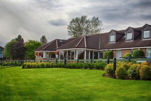 Uma casa residencial com gramado bem cuidado, cerca de piquete e jardim com diversas plantas e flores.