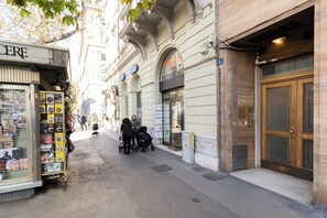 Rua com um quiosque vendendo postais e um edifício com uma grande porta de madeira.