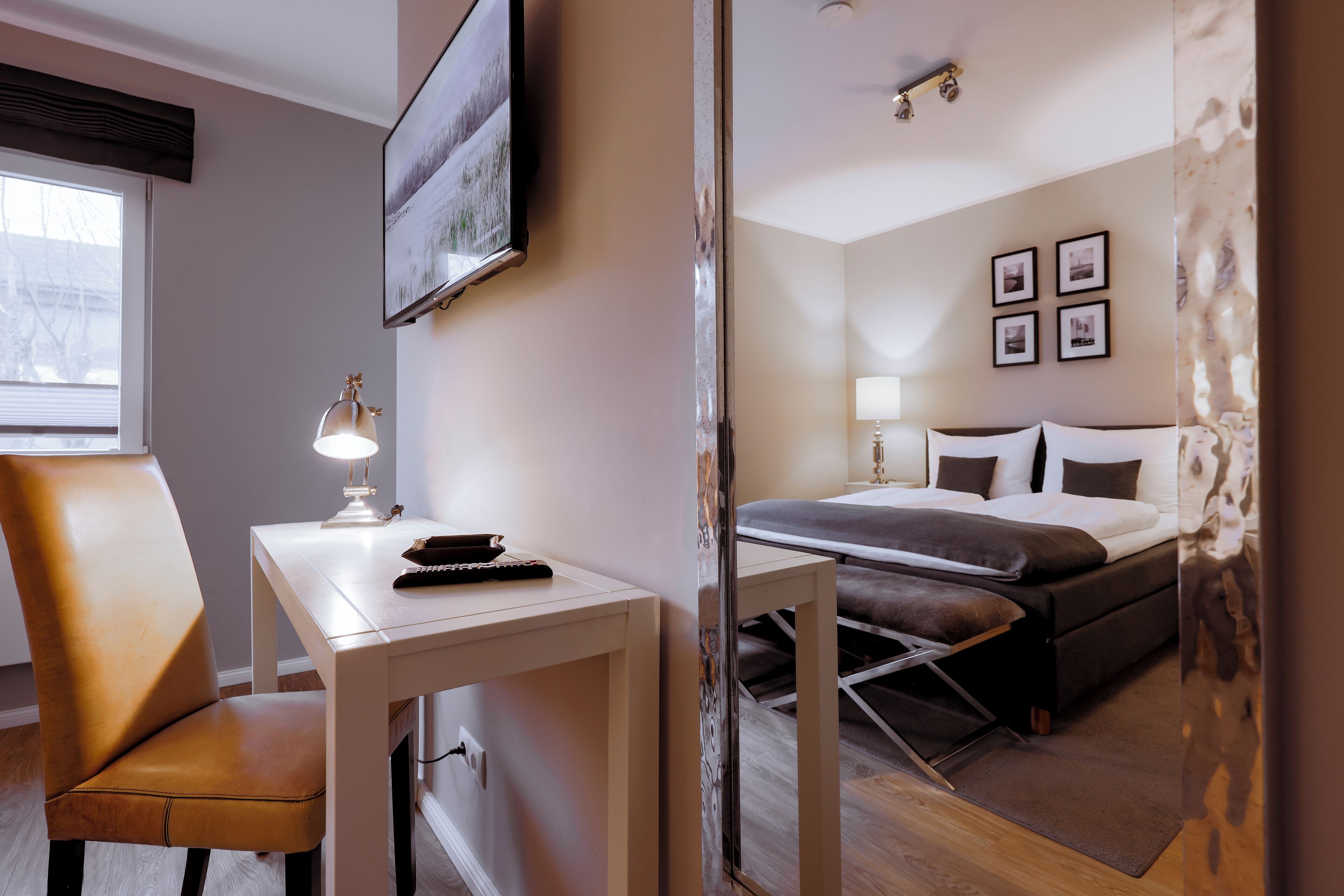 Quarto de hotel com cama, mesa de cabeceira, cadeira e escrivaninha com abajur.