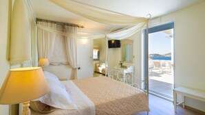 Quarto com cama, mesa de cabeceira, luminária, TV e vista para a praia.