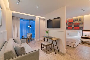 Quarto de hotel moderno com sofá, uma mesa pequena, televisão na parede e uma cama.