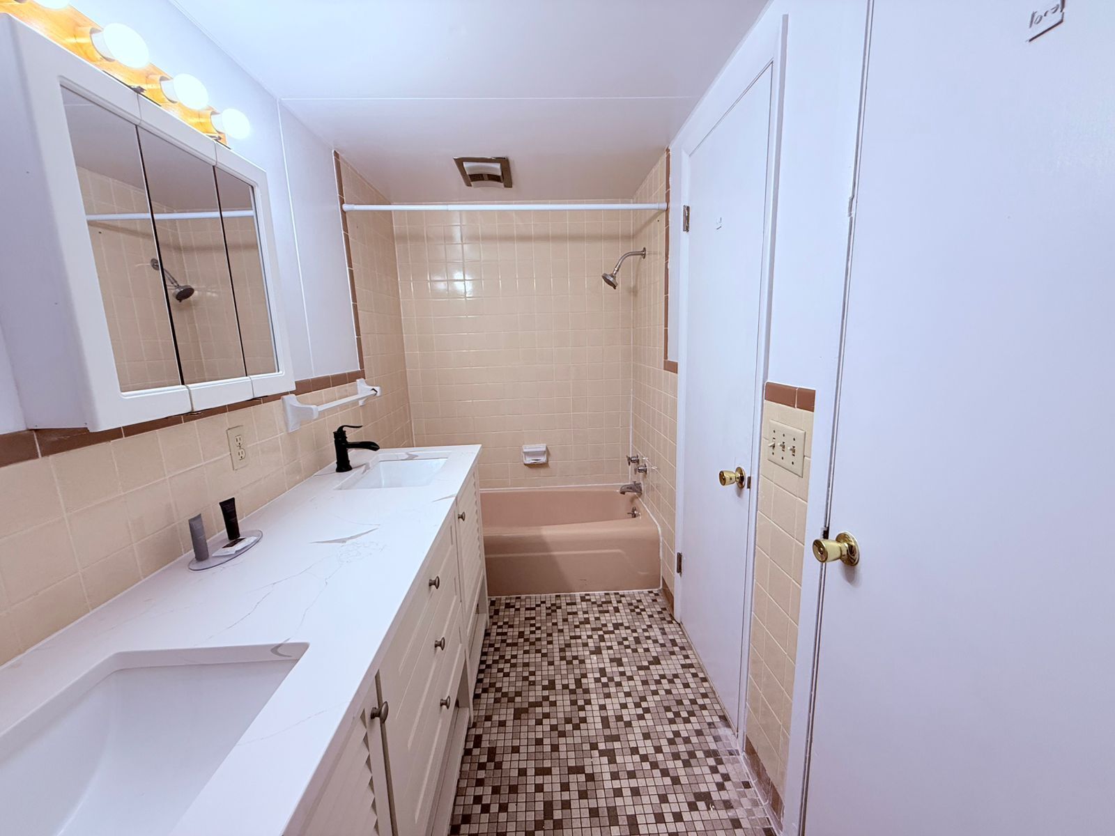 Casa de banho compacta com lavatório branco, espelho, chuveiro e chão em mosaico.