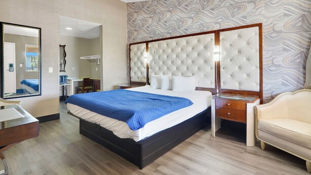 Quarto de hotel com cama grande, mesa de cabeceira, cadeira, escrivaninha e espelho.