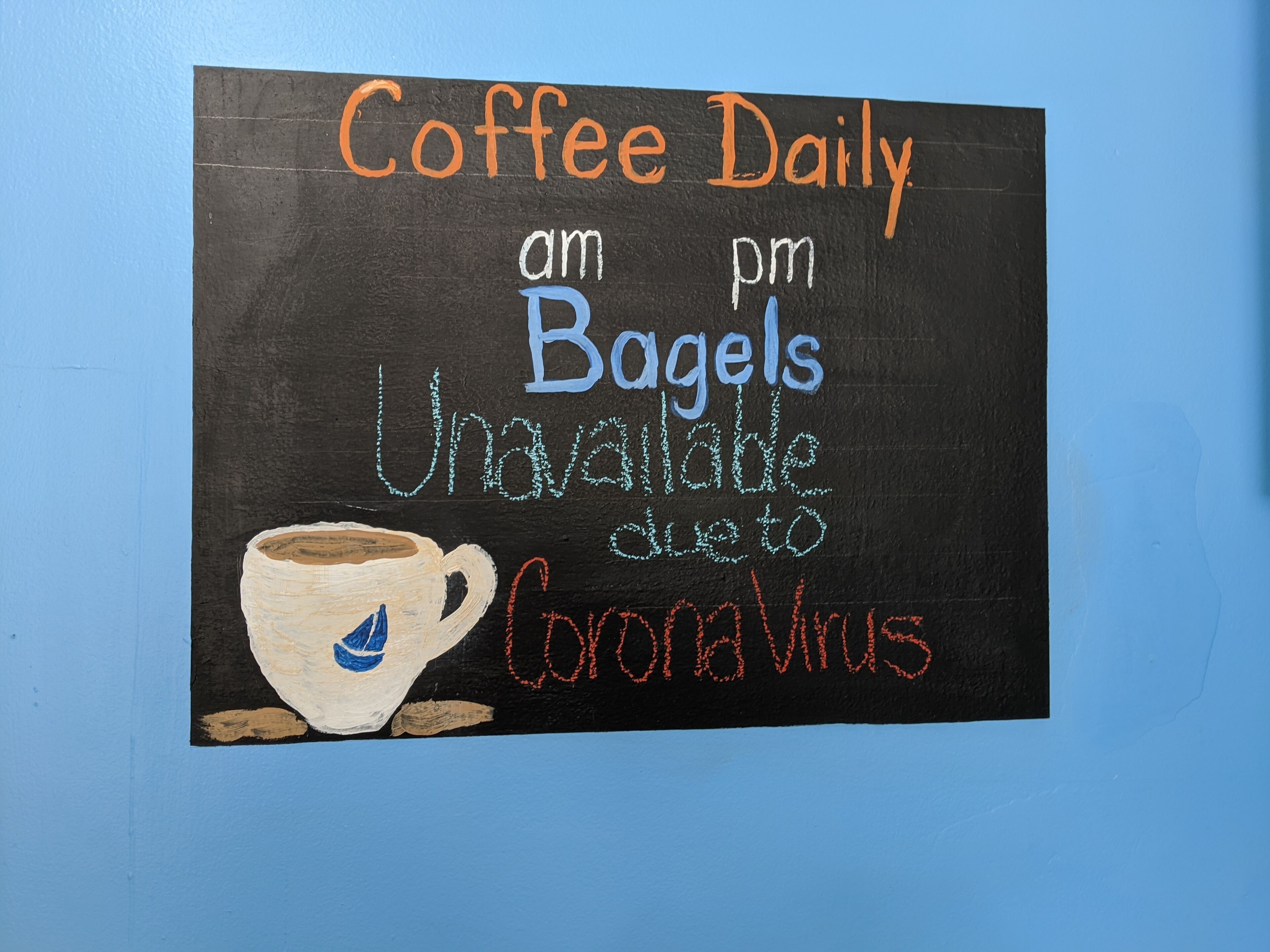 Um aviso com o texto: 'Café diariamente, abre e fecha. Bagels indisponíveis devido à Coronavirus.'