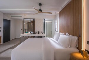 Quarto de hotel com cama, escrivaninha, cadeira, espelho e ventilador de teto.