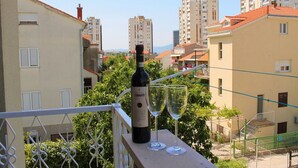 Varanda com uma garrafa de vinho Chianti e duas taças, com vista para uma área residencial com edifícios e vegetação.