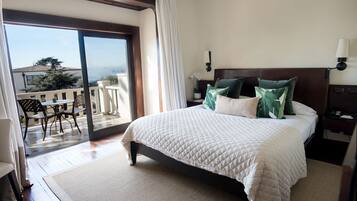 Quarto de hotel com uma cama grande, mesa de cabeceira, luminária e vista para o exterior.