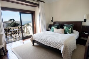 Quarto de hotel com uma cama grande, mesa de cabeceira, luminária e vista para o exterior.