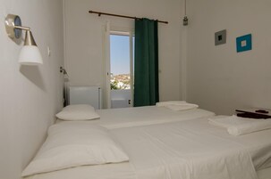 Quarto de hotel com duas camas, janela com vista, luminária e pequena mesa com um objeto vermelho em cima.