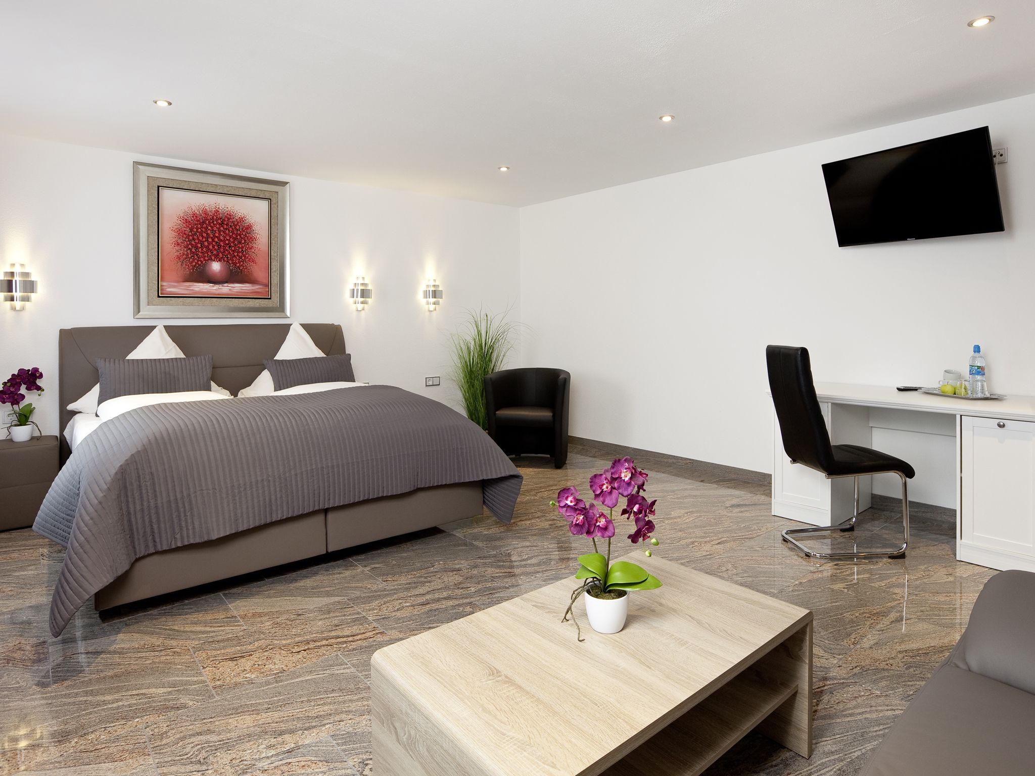 Quarto de hotel moderno com uma cama, uma escrivaninha, uma cadeira e uma televisão na parede.