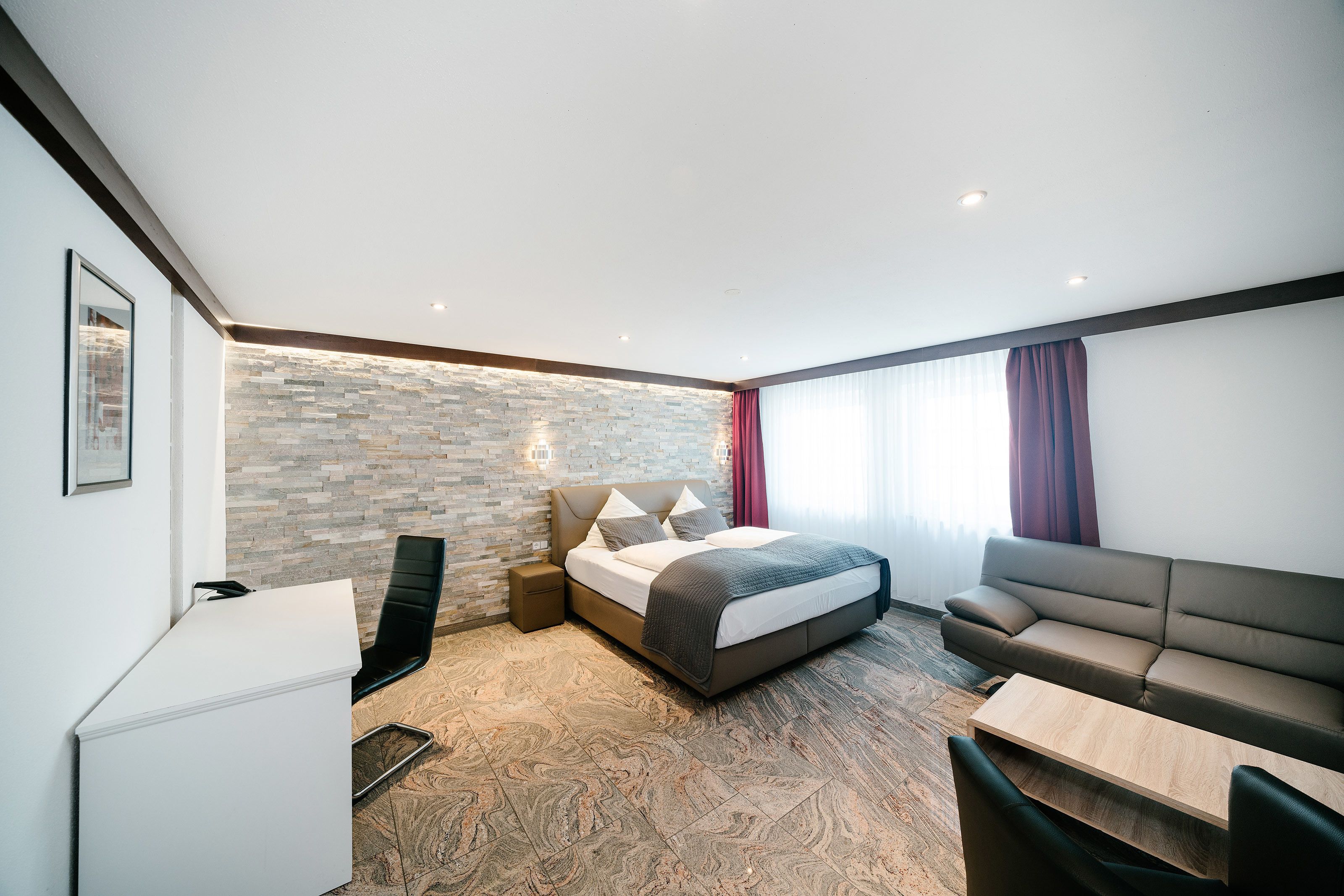 Quarto de hotel moderno com cama, sofá, escrivaninha e uma pequena mesa.