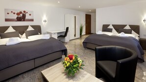 Quarto de hotel com duas camas, uma escrivaninha, uma cadeira e uma mesa de centro com flores.