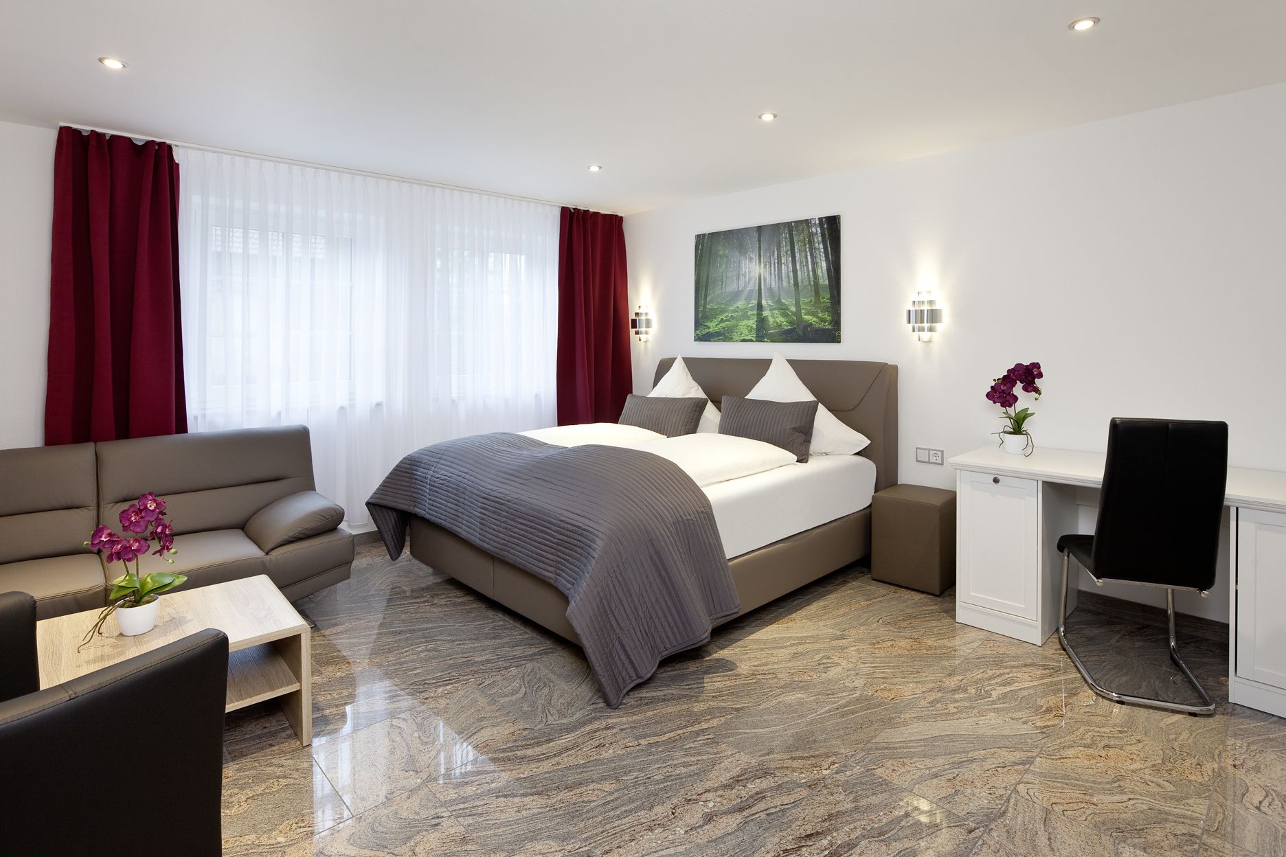 Quarto de hotel moderno com uma cama grande, um sofá, uma escrivaninha e uma pintura na parede.