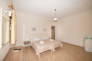 Quarto de hotel com duas camas, uma escrivaninha, uma mesa de cabeceira, um espelho e uma pequena cozinha equipada.
