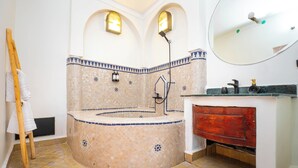 Um banheiro com banheira, uma escada de madeira, um espelho e piso de azulejos.