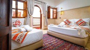 Quarto de hotel com duas camas, um tapete estampado e vista através de uma porta aberta.