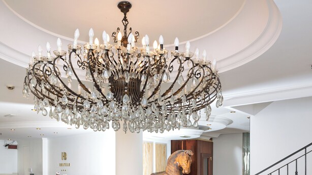 Um hall amplo com um sofá de couro vermelho, uma mesa de centro de vidro, um lustre e uma estátua de cavalo.