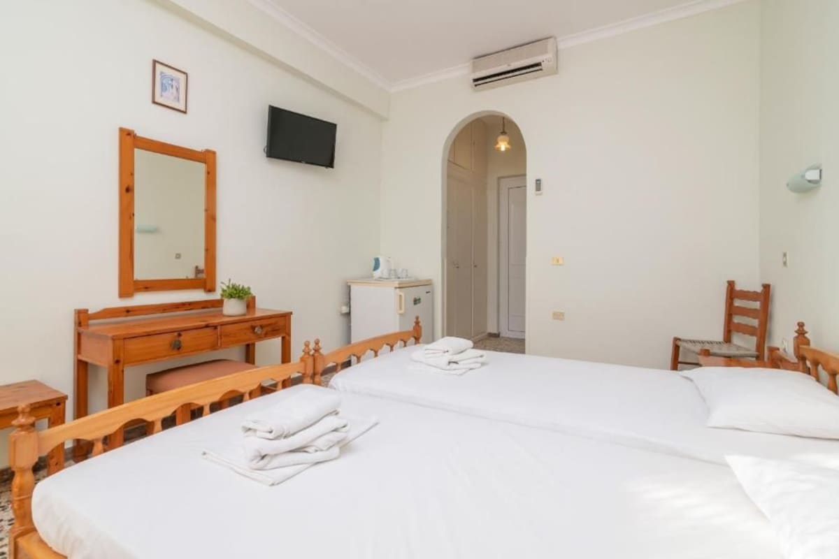 Quarto de hotel com duas camas, cómoda de madeira, televisão e unidade de ar condicionado.
