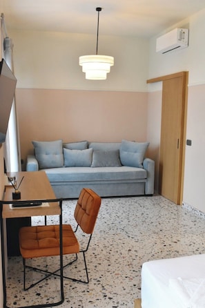 Quarto com sofá, escrivaninha com cadeira, cama, luminária pendente e ar condicionado.