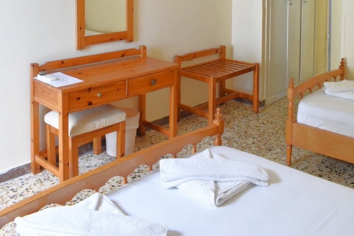 Quarto de hotel com secretária de madeira, televisão, ar condicionado, cama e guarda-roupa.
