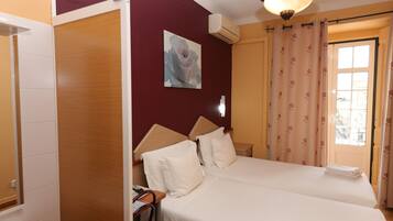 Quarto de hotel com duas camas, banheiro e janela com cortinas florais.