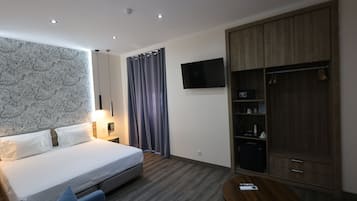 Quarto de hotel moderno com uma cama grande, um guarda-roupa de madeira, uma TV na parede e uma pequena mesa.