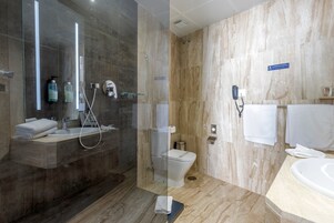 Uma casa de banho moderna com chuveiro em cabine de vidro, parede de mármore, sanita e lavatório.
