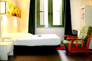 Quarto com uma cama, uma cadeira, uma escrivaninha e uma janela com persianas verdes.