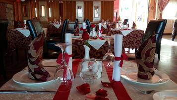 Restaurante com mesas preparadas para refeições, decorado com rosas vermelhas e guardanapos brancos amarrados com fitas vermelhas.
