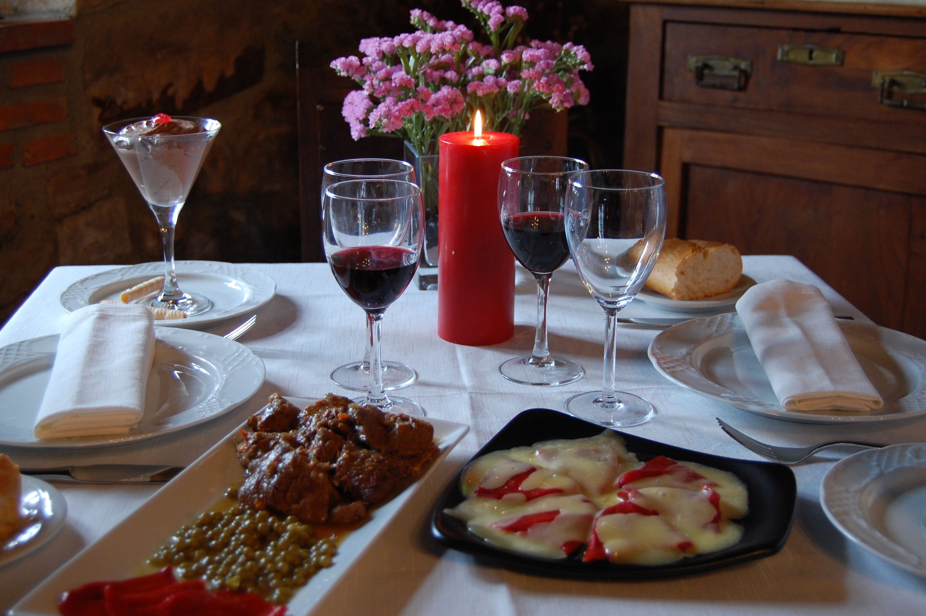 Mesa posta para refeição, com pratos de comida, copos de vinho e uma vela acesa.
