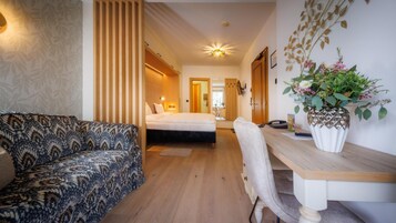 Quarto de hotel acolhedor com um sofá estampado, uma cama, uma escrivaninha com telefone e uma planta decorativa.