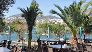 Um café ao ar livre com móveis de vime e vista para o mar e uma cidade na colina.