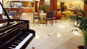 Um piano de cauda num saguão de hotel, com bar e área de estar.