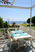 Uma área de refeições ao ar livre coberta, com uma mesa posta para dois, com vista para uma praia e o mar.
