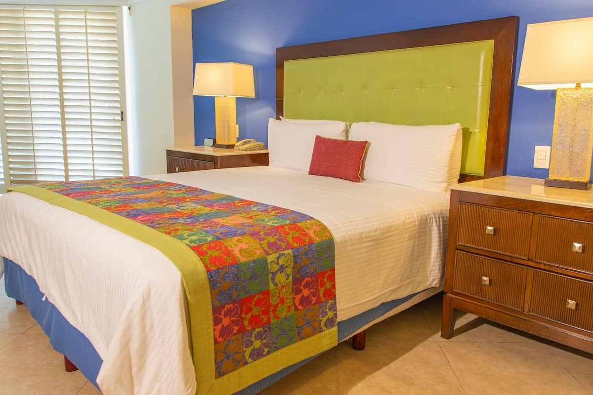 Quarto de hotel com cama, mesa de cabeceira, cômoda e janela com persianas.