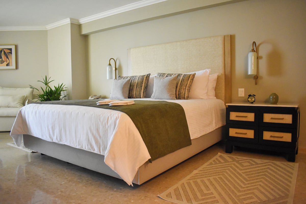 Quarto com cama, mesas de cabeceira, luminária e planta.